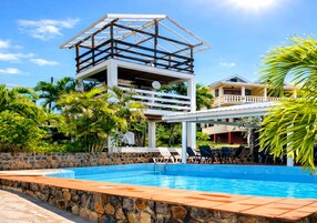 Uma piscina com espreguiçadeiras, um muro de pedra e um edifício com varanda.