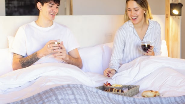 Um casal sentado na cama com uma bandeja de comida e bebidas.