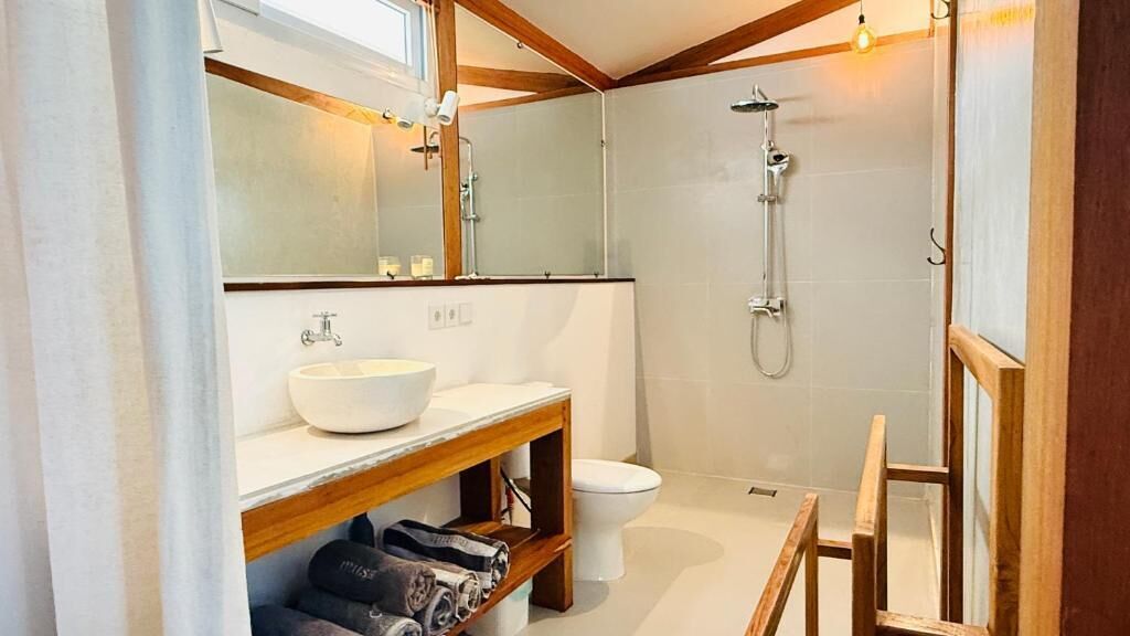 Uma casa de banho moderna com um espelho grande, uma sanita branca, um lavatório e um chuveiro.