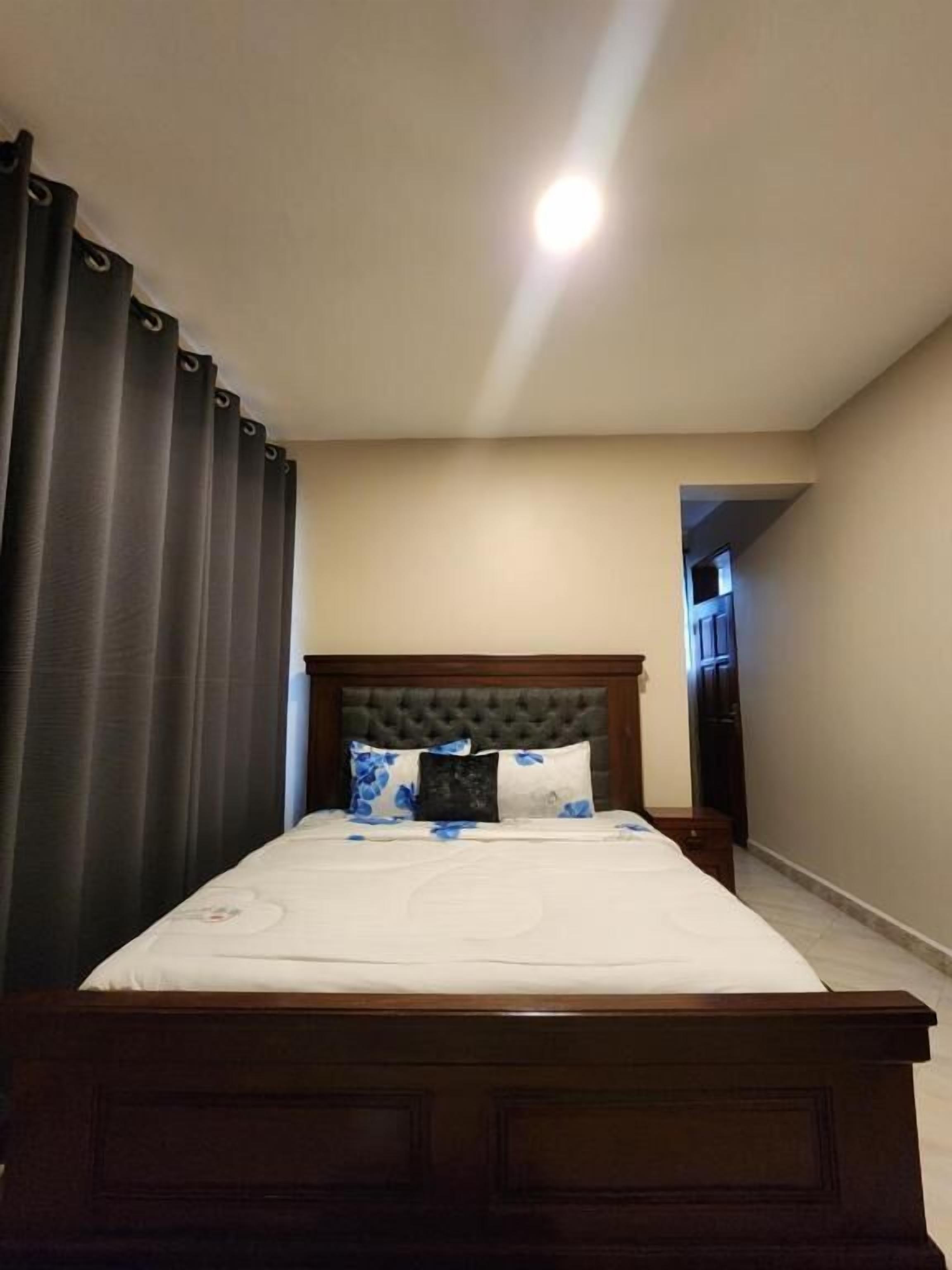 Quarto com cama, cortinas escuras, cabeceira e mesa de cabeceira.
