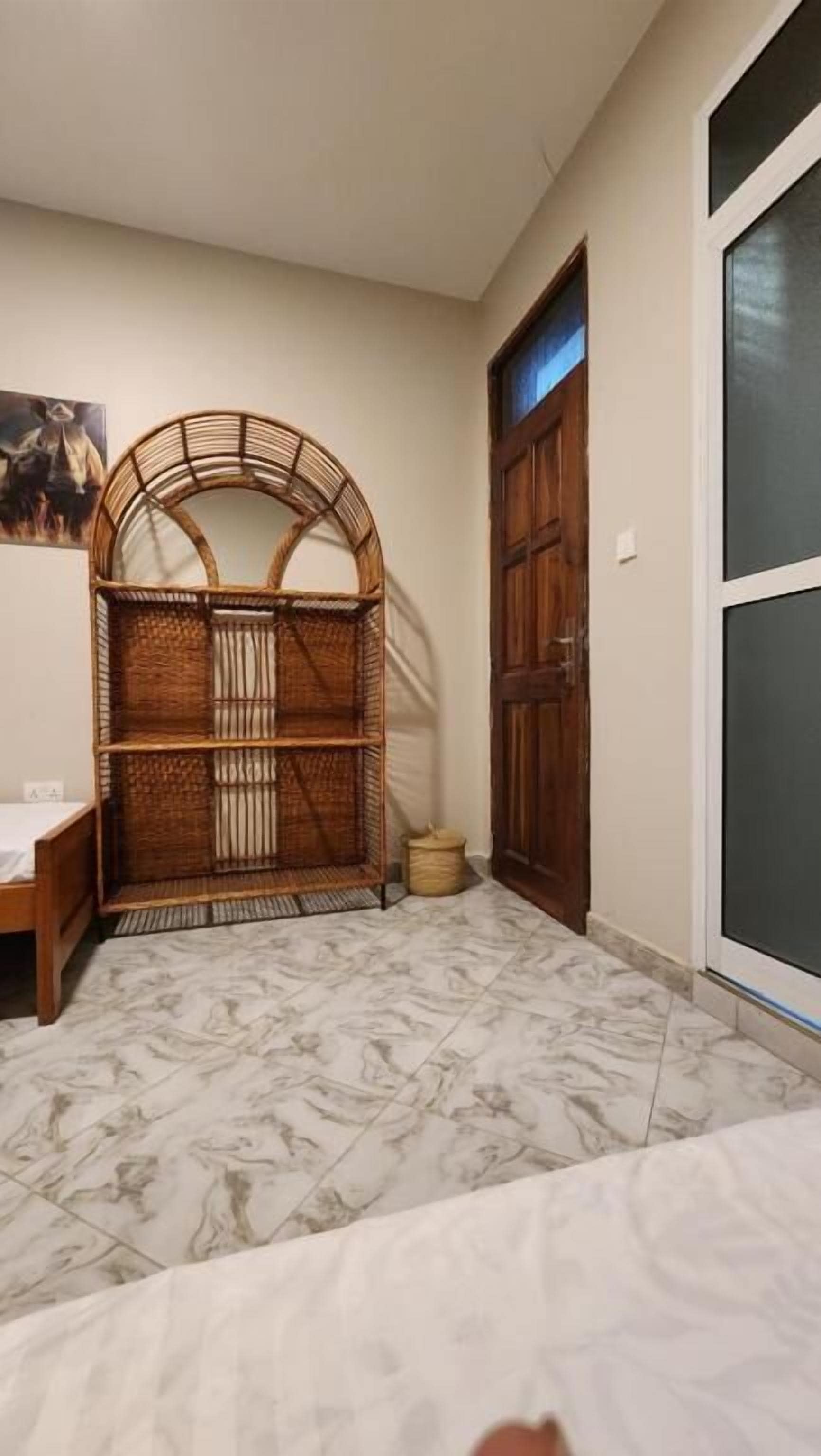 Quarto com uma cama, um guarda-roupa de madeira, uma cadeira de vime e um quadro na parede.