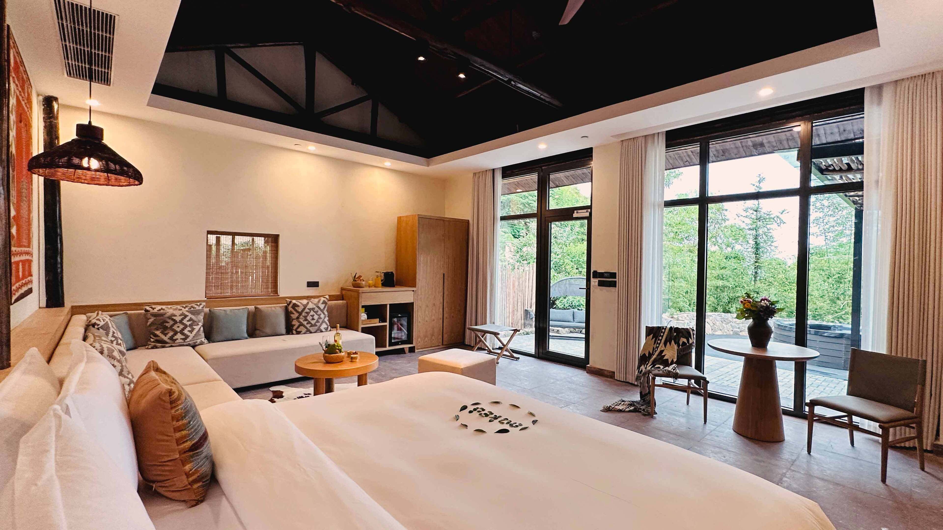 Um quarto espaçoso com uma cama grande, um sofá, uma mesinha e vista para o exterior por grandes janelas.