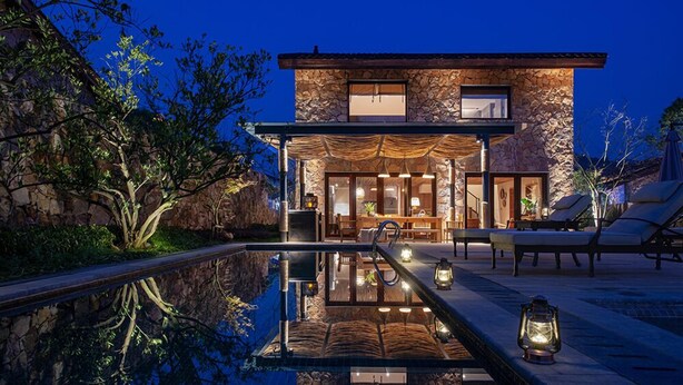 Uma casa moderna com fachada de pedra, piscina e área de estar ao ar livre.