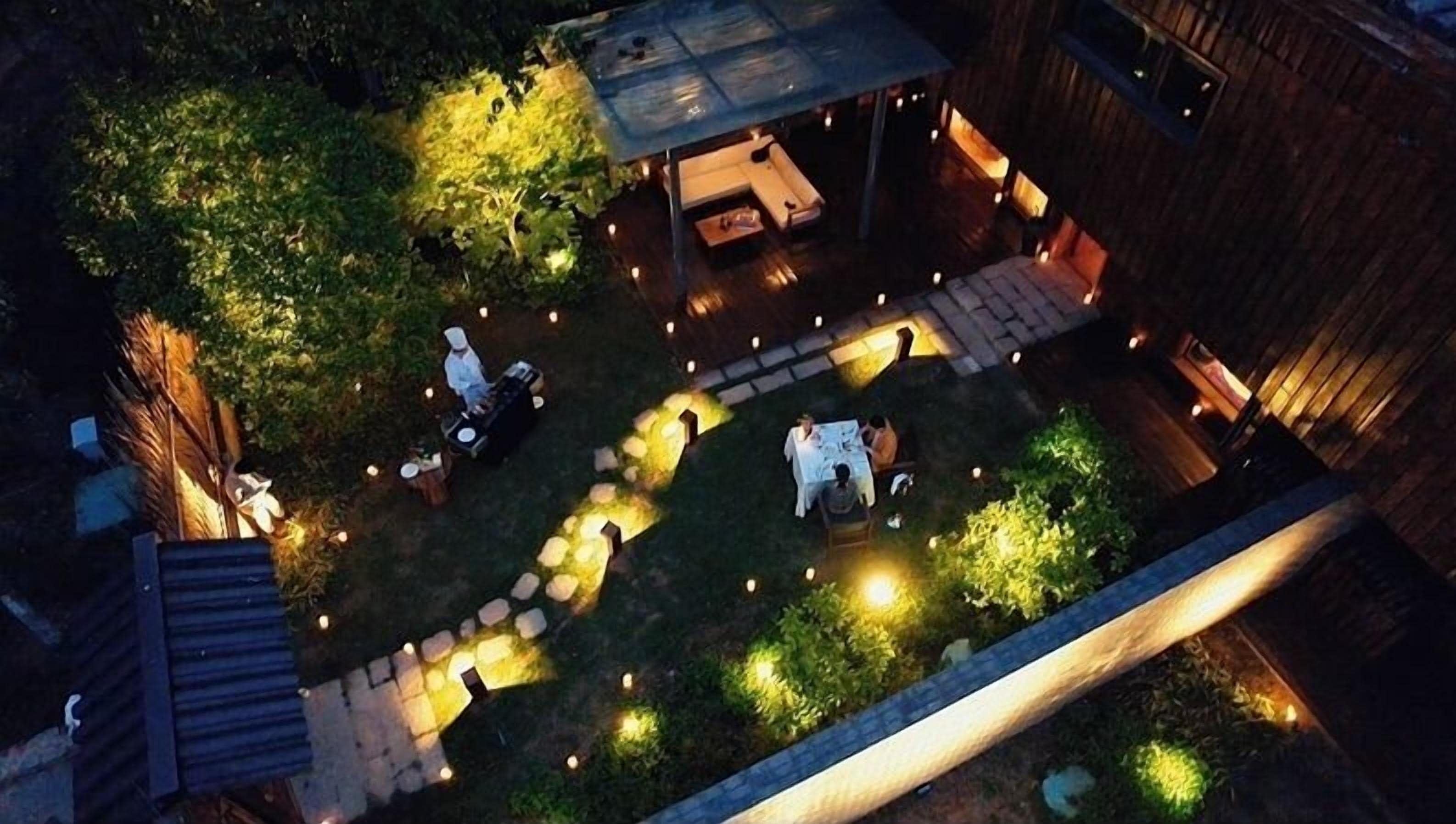 Uma área de estar ao ar livre com um deck de madeira, assentos e iluminação ambiente.