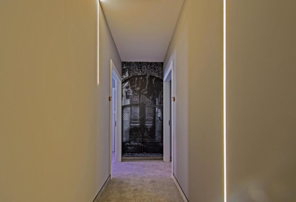 Um corredor estreito com piso revestido de carpete conduz a um quarto com parede estampada em preto e branco.