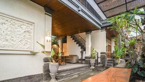 Um pátio balinês tradicional com uma mesa de madeira e bancos, uma escadaria e um grande relevo na parede.