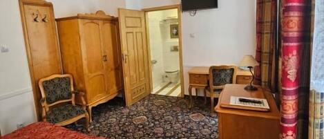Quarto de hotel com cama, escrivaninha, guarda-roupa e televisão.