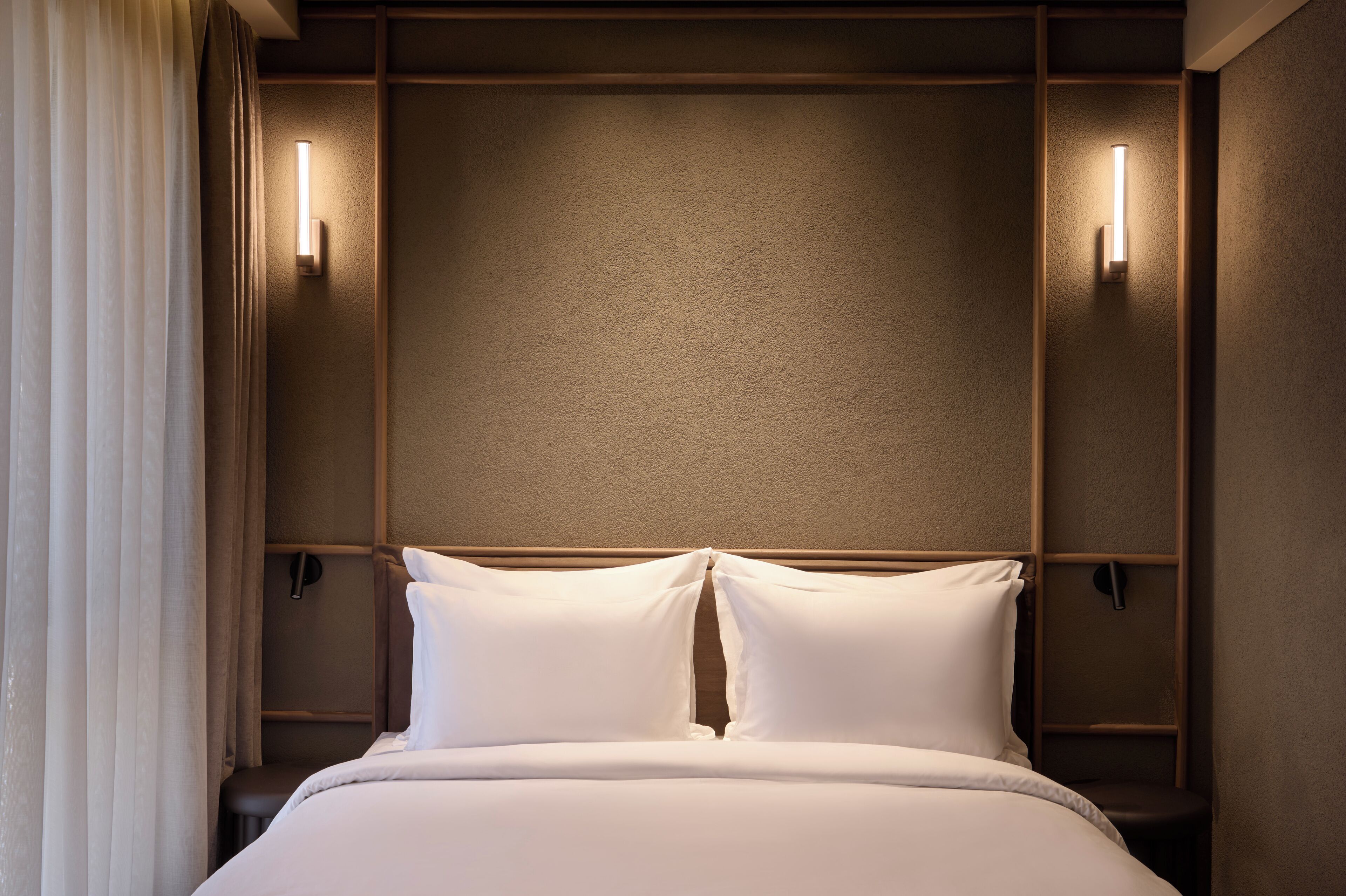 Quarto de hotel com cama, cortinas e iluminação embutida na parede.