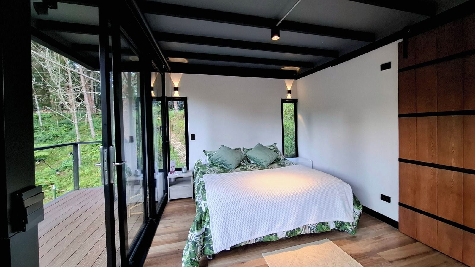Quarto com cama, mesa de cabeceira e vista para o exterior.