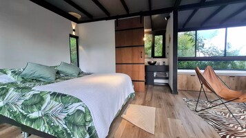 Quarto com cama, cadeira, mesinha e janela.