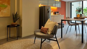 Uma sala de estar moderna com um sofá, uma mesa de jantar e uma área de cozinha com geladeira e armários.