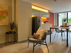 Uma sala de estar moderna com um sofá, uma mesa de jantar e uma área de cozinha com geladeira e armários.