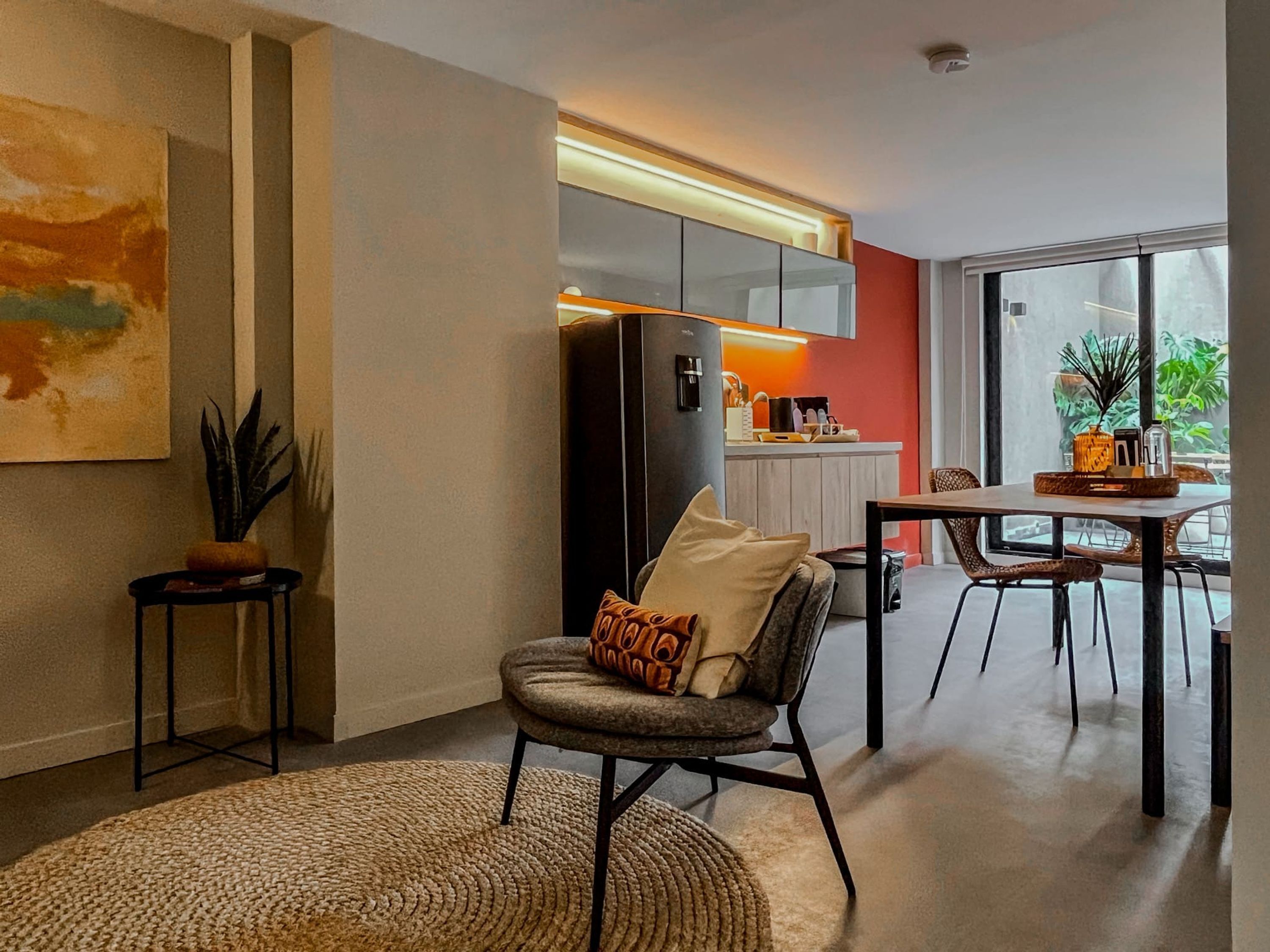 Uma sala de estar moderna com sofá, mesa de jantar e área de cozinha com geladeira e armários.