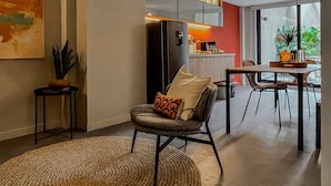 Uma sala de estar moderna com sofá, mesa de jantar e área de cozinha com geladeira e armários.