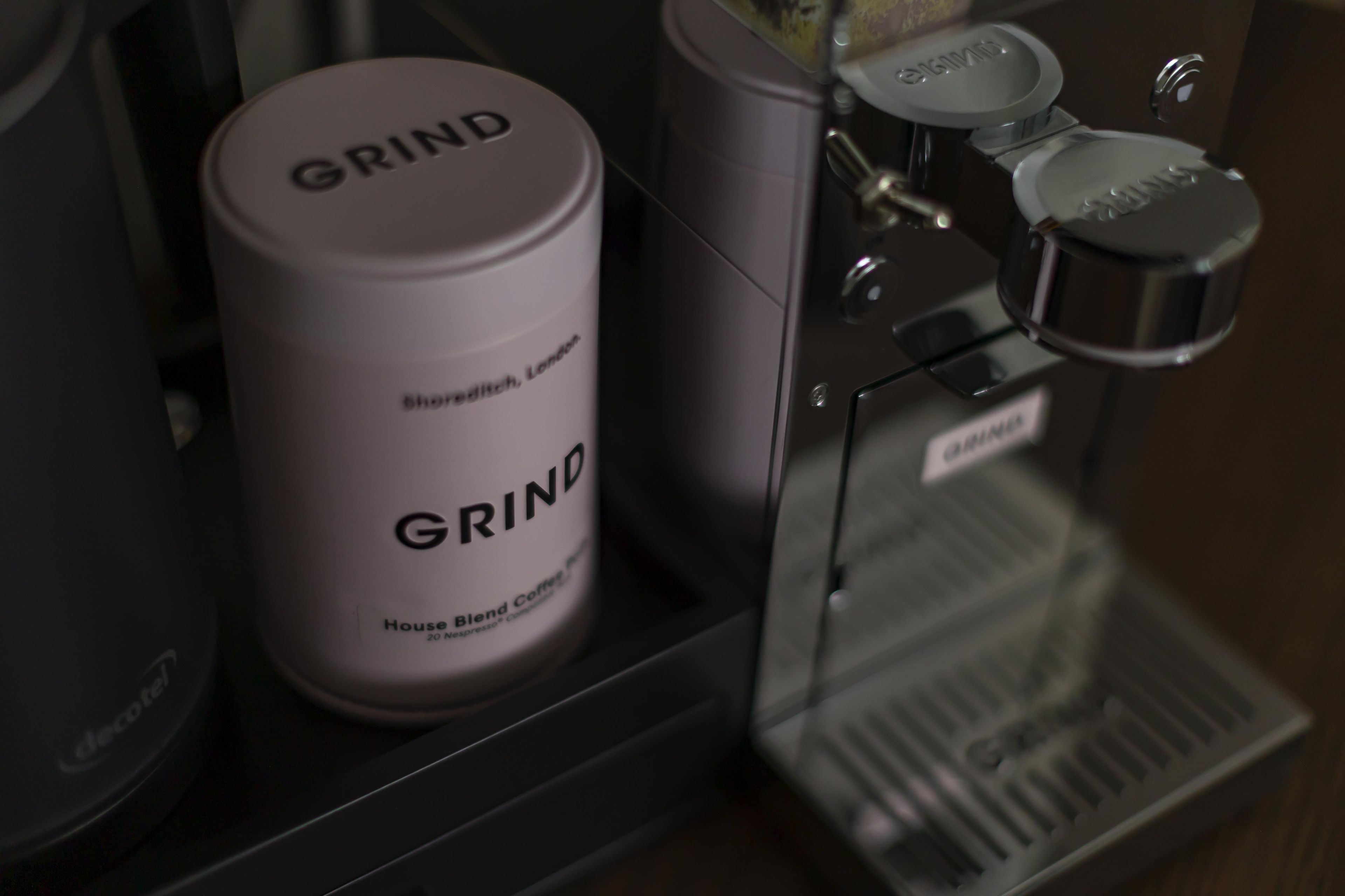 Máquina de café com recipiente rotulado 'GRIND' e suporte para cápsulas de café.