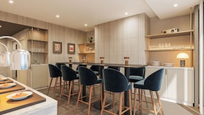 Uma cozinha moderna com área de jantar, apresentando uma mesa de madeira, cadeiras escuras e um balcão com banquetas.