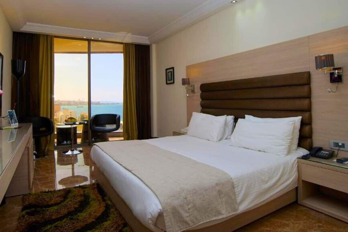 Quarto de hotel com cama, escrivaninha, cadeira, televisão e vista para o mar.