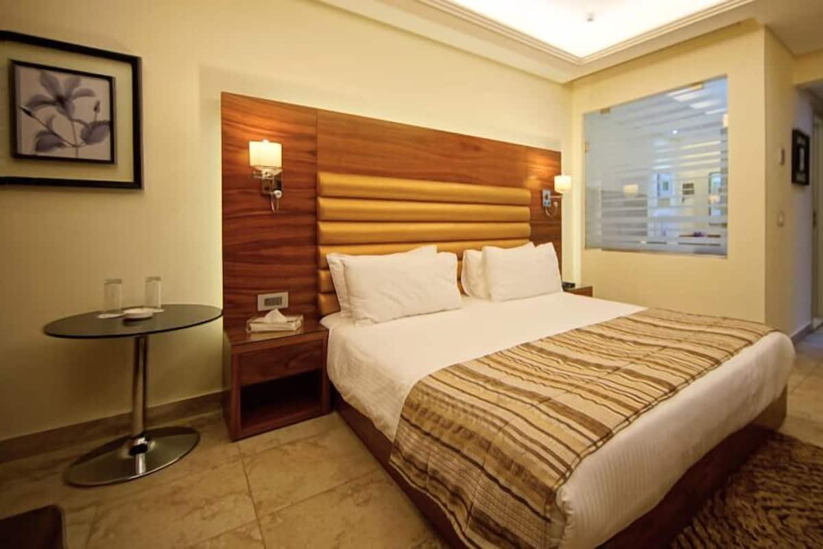 Quarto de hotel com cama, abajures, uma mesinha redonda e uma janela com persianas.