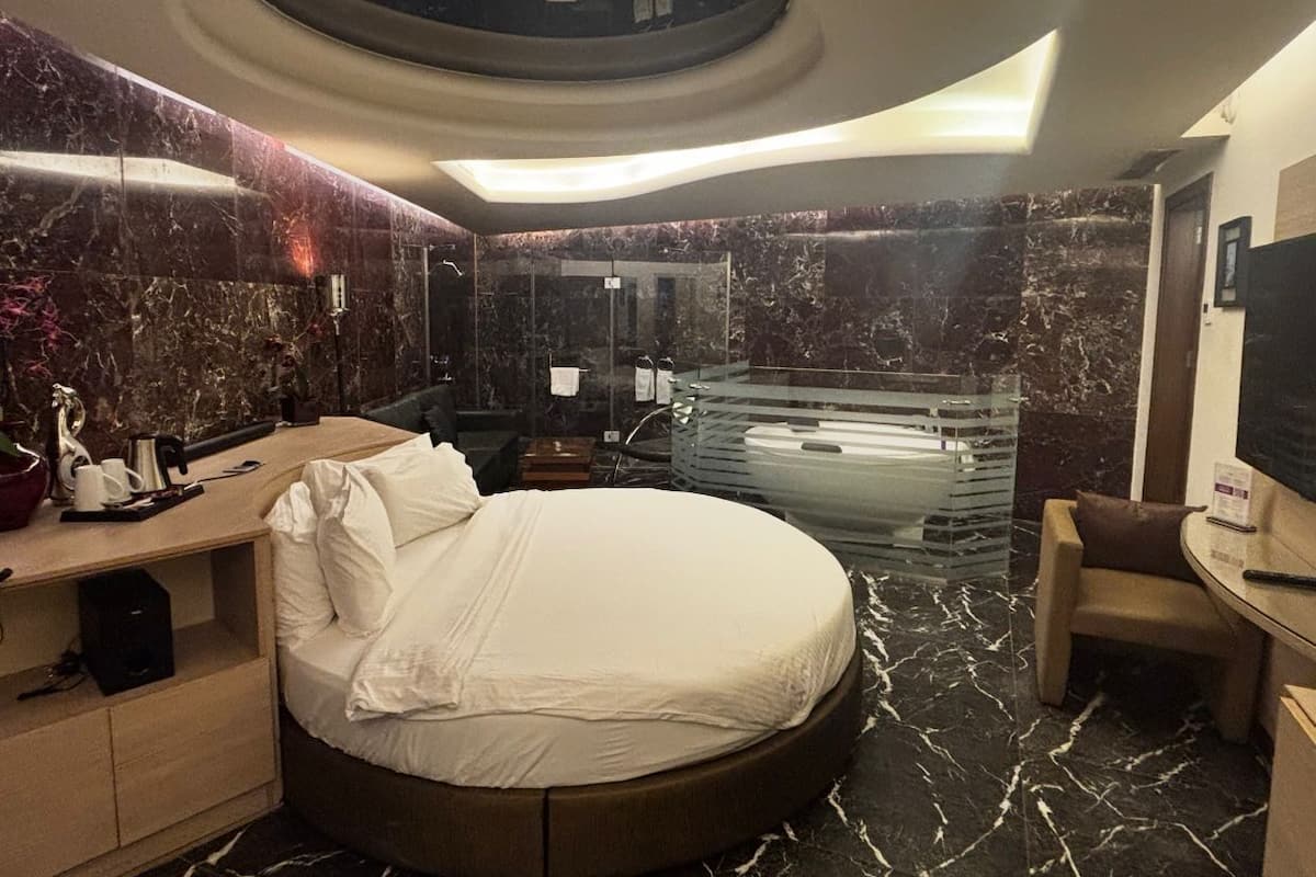 Quarto de hotel moderno com cama redonda, escrivaninha, poltrona, banheira e paredes de mármore.