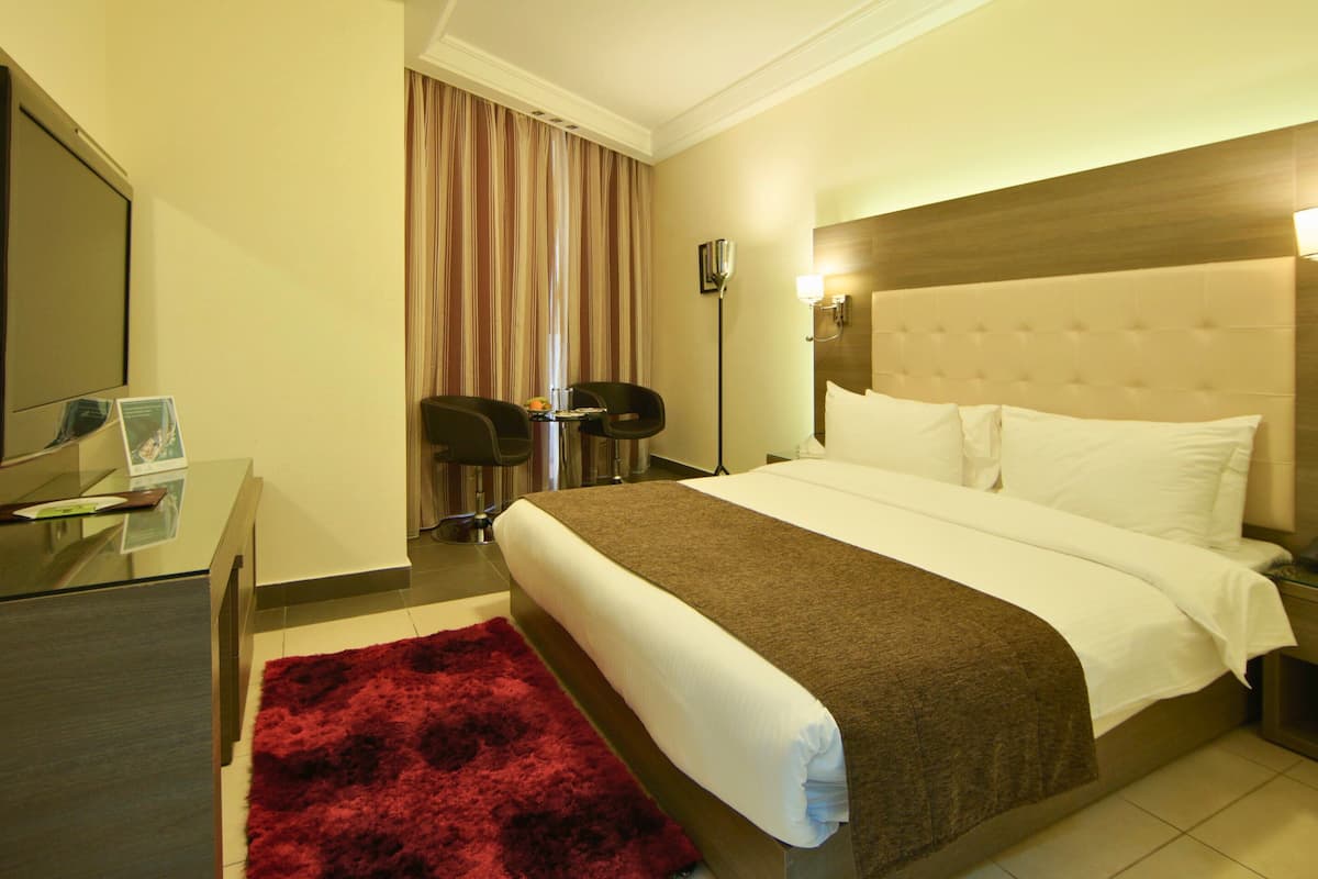 Quarto de hotel com uma cama grande, uma escrivaninha, uma cadeira, uma TV e um tapete vermelho.