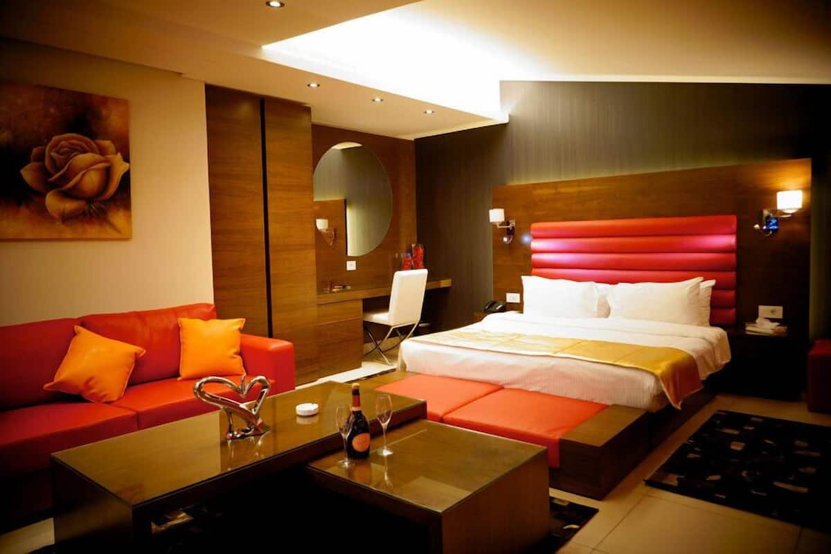 Quarto de hotel moderno com uma cama grande, um sofá vermelho, uma mesa de centro de madeira e um espelho fixado na parede.