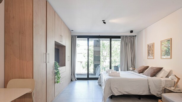 Quarto moderno com cama, mesa de cabeceira e vista através de uma grande janela.