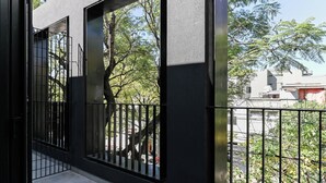 Uma varanda com guarda-corpo de metal, vista para árvores e edifícios, e céu claro.