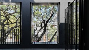 Visão através de um portão de metal preto, com árvores e um edifício ao fundo.
