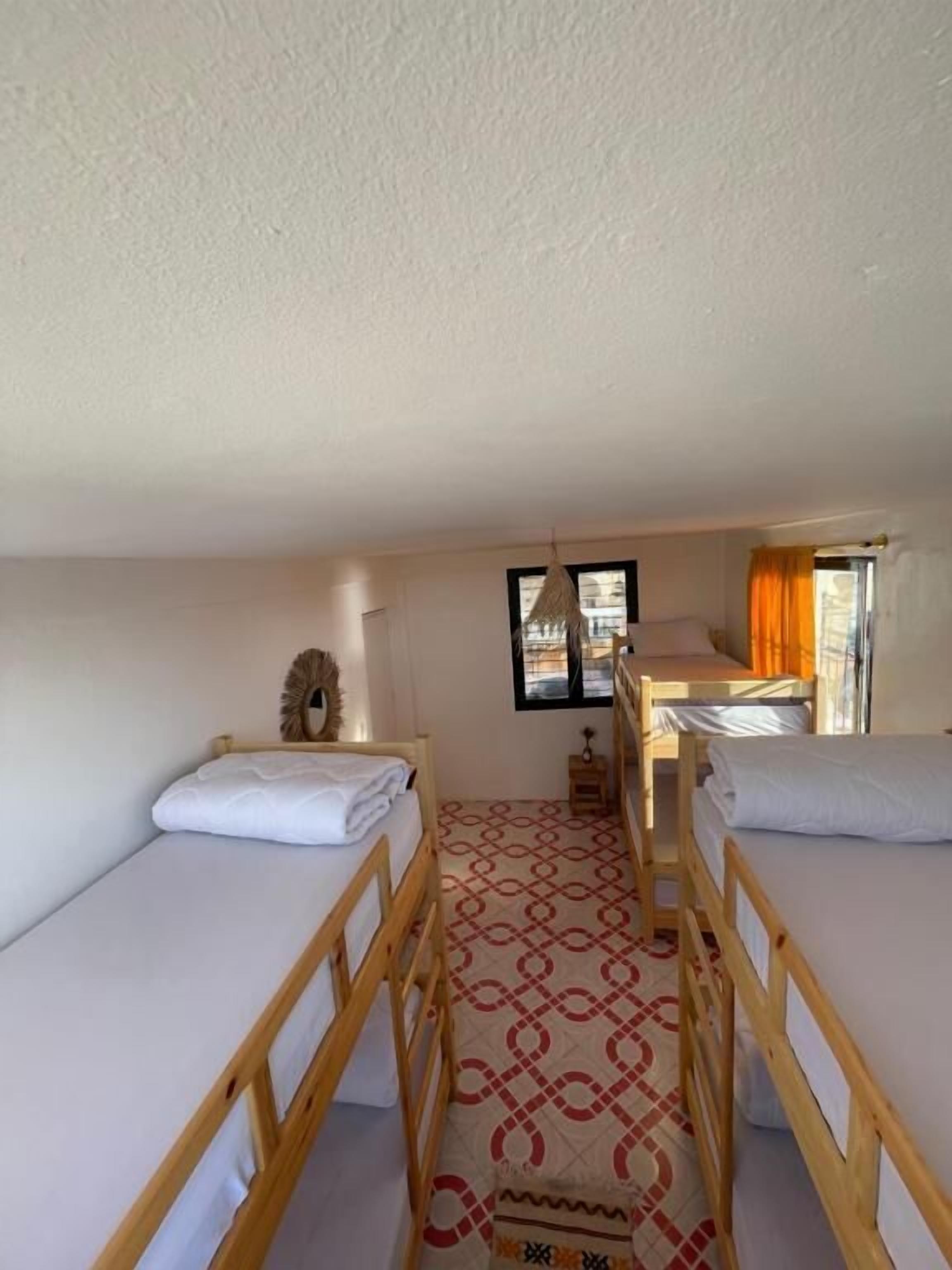Um quarto em dormitório com três beliches de madeira, um chão estampado e uma janela com cortinas.