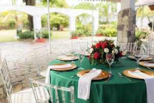 Mesa posta para refeição com toalha de mesa verde, guardanapos brancos e arranjo floral.