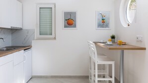 Uma cozinha compacta com armários brancos, bancada de mármore, uma pequena mesa de jantar com cadeiras e duas quadros na parede.