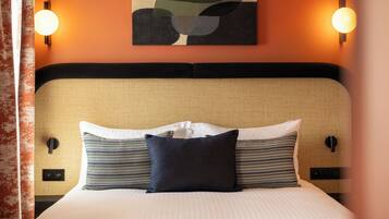 Quarto de hotel com cama, duas arandelas, cabeceira e uma obra de arte na parede.