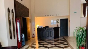 Uma área de recepção com piso xadrez, um balcão de atendimento, um relógio e um extintor de incêndio.
