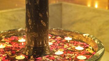 Uma bacia de pedra com uma coluna central, rodeada por velas e pétalas de rosa.