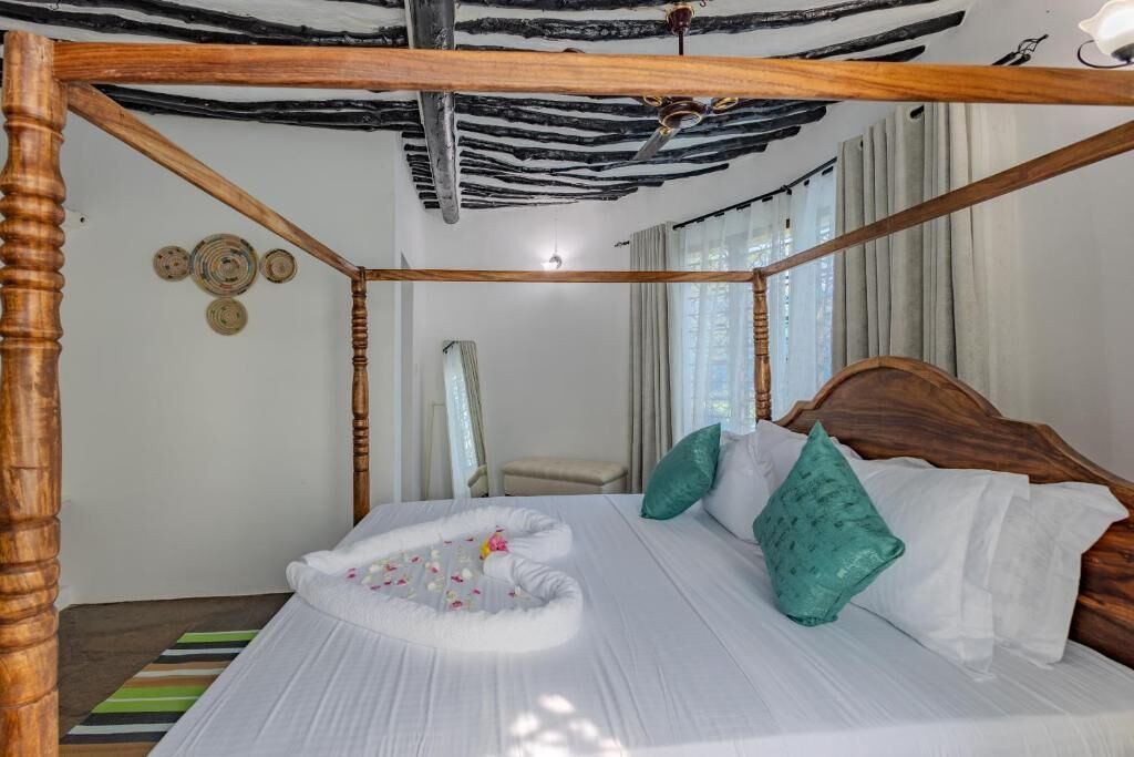 Uma cama de dossel com estrutura de madeira, roupa de cama branca e almofadas verdes.