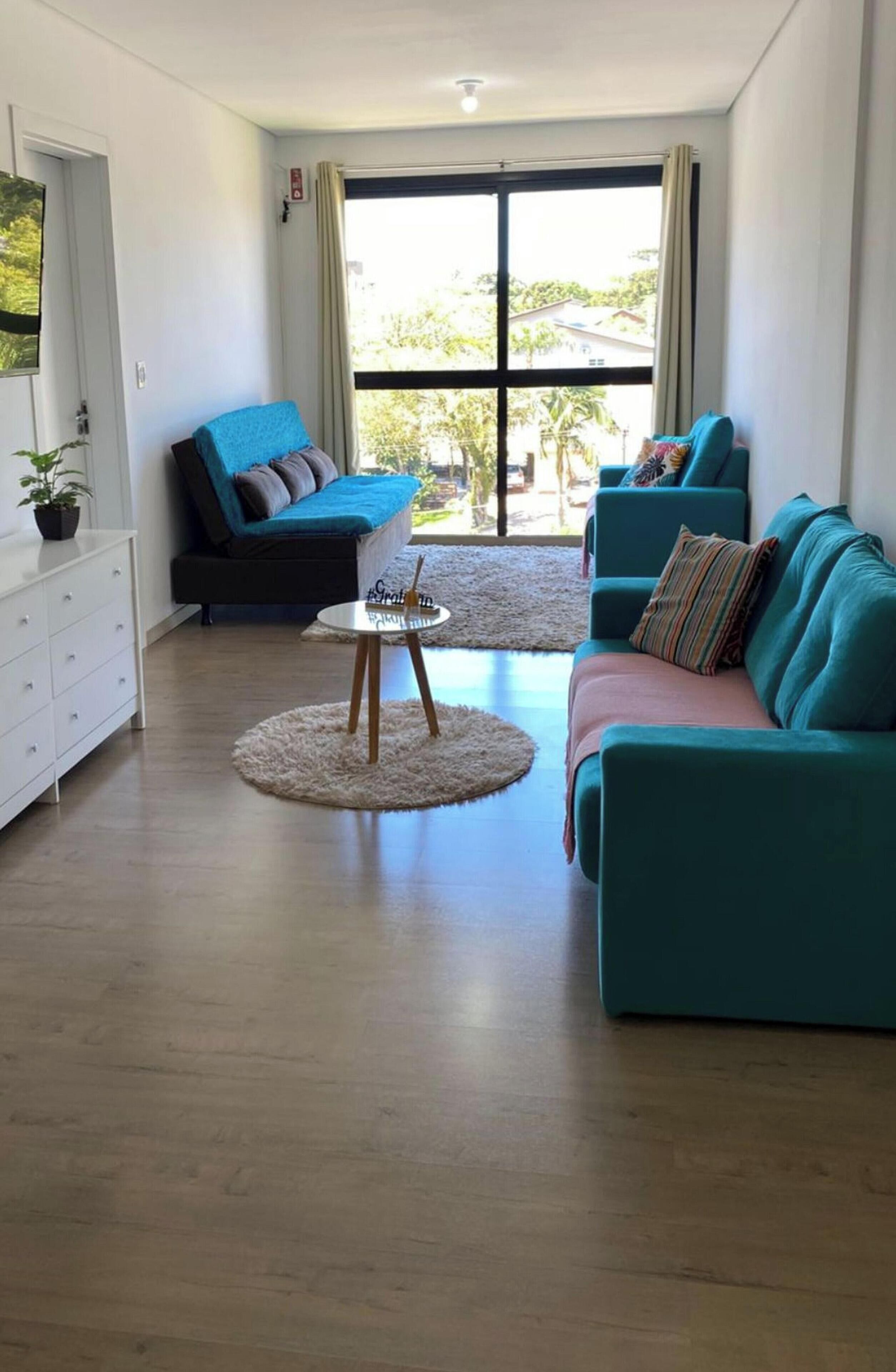 Uma sala de estar moderna com um sofá, uma mesa de centro e uma vista através de janelas amplas.