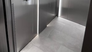 Um elevador moderno com portas metálicas, um visor digital e um corrimão.