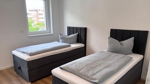 Quarto com duas camas, janela e piso de madeira.