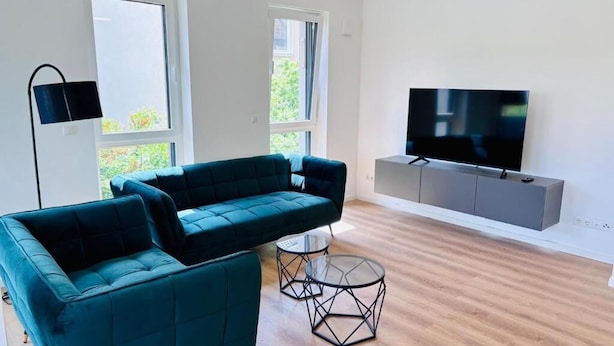 Uma sala de estar moderna com um sofá azul-turquesa, uma mesa de centro de vidro, uma TV de tela plana e um armário minimalista.