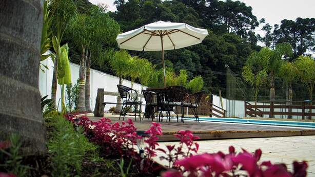 Uma área de piscina ao ar livre com deck de madeira, mesa e cadeiras, e um grande guarda-sol.