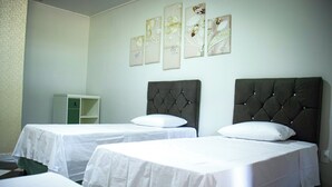 Duas camas de solteiro com roupa de cama branca, um pequeno armário verde e um quadro de parede com motivos florais.