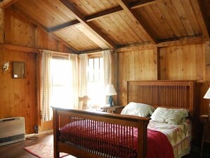Quarto de cabana de madeira com cama, mesa de cabeceira, luminária e radiador.