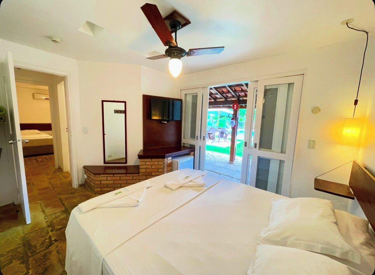 Quarto de hotel com cama, ventoinha no teto, televisão e vista para o exterior.