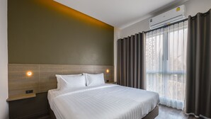 Quarto de hotel moderno com uma cama grande, cabeceira de madeira, ar condicionado fixado na parede e uma janela com cortinas.