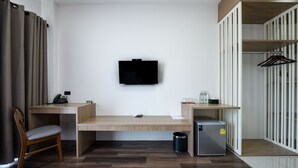 Quarto de hotel com escrivaninha de madeira, uma cadeira, televisão fixada na parede, mini-frigorífico e porta-casacos.