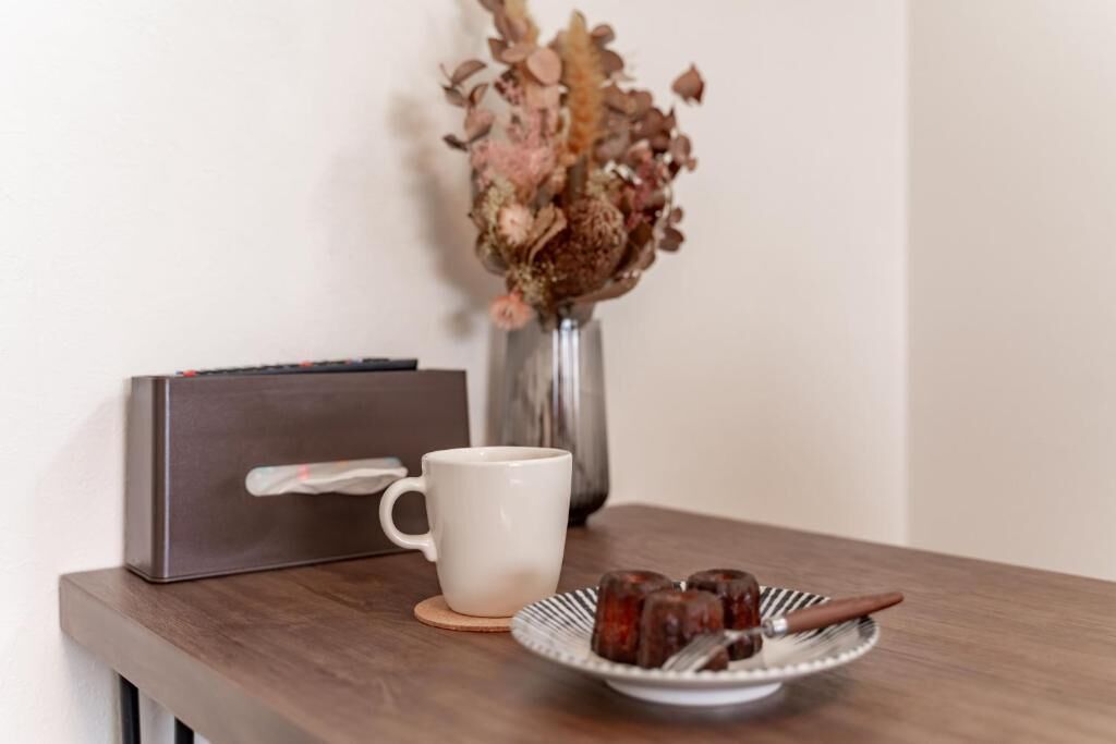 Uma mesa com uma caneca branca, um prato com comida e um vaso com flores secas.