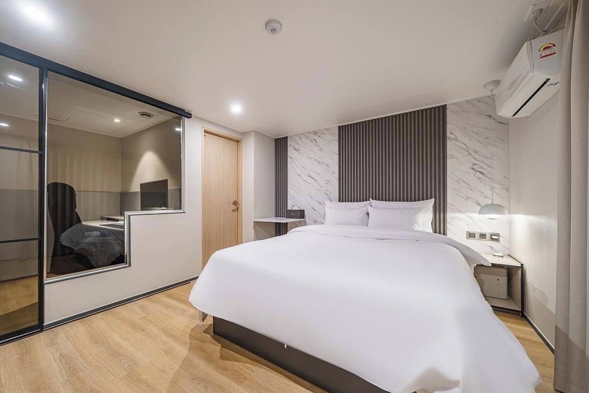 Quarto de hotel moderno com uma cama grande, um painel de separação de vidro, uma parede com padrão marmorizado e um aparelho de ar condicionado.