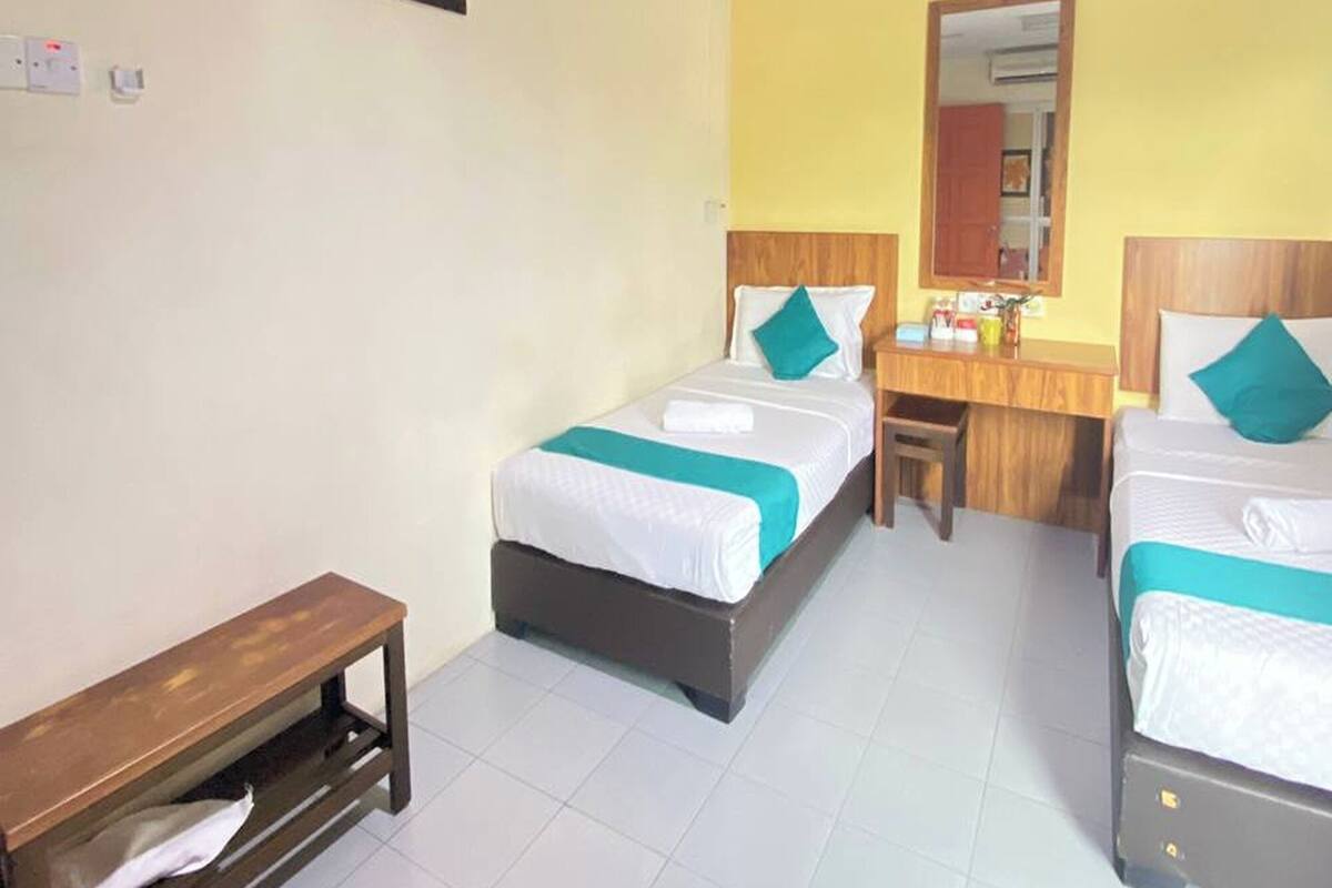 Quarto de hotel com duas camas, uma escrivaninha, um banco e um espelho.