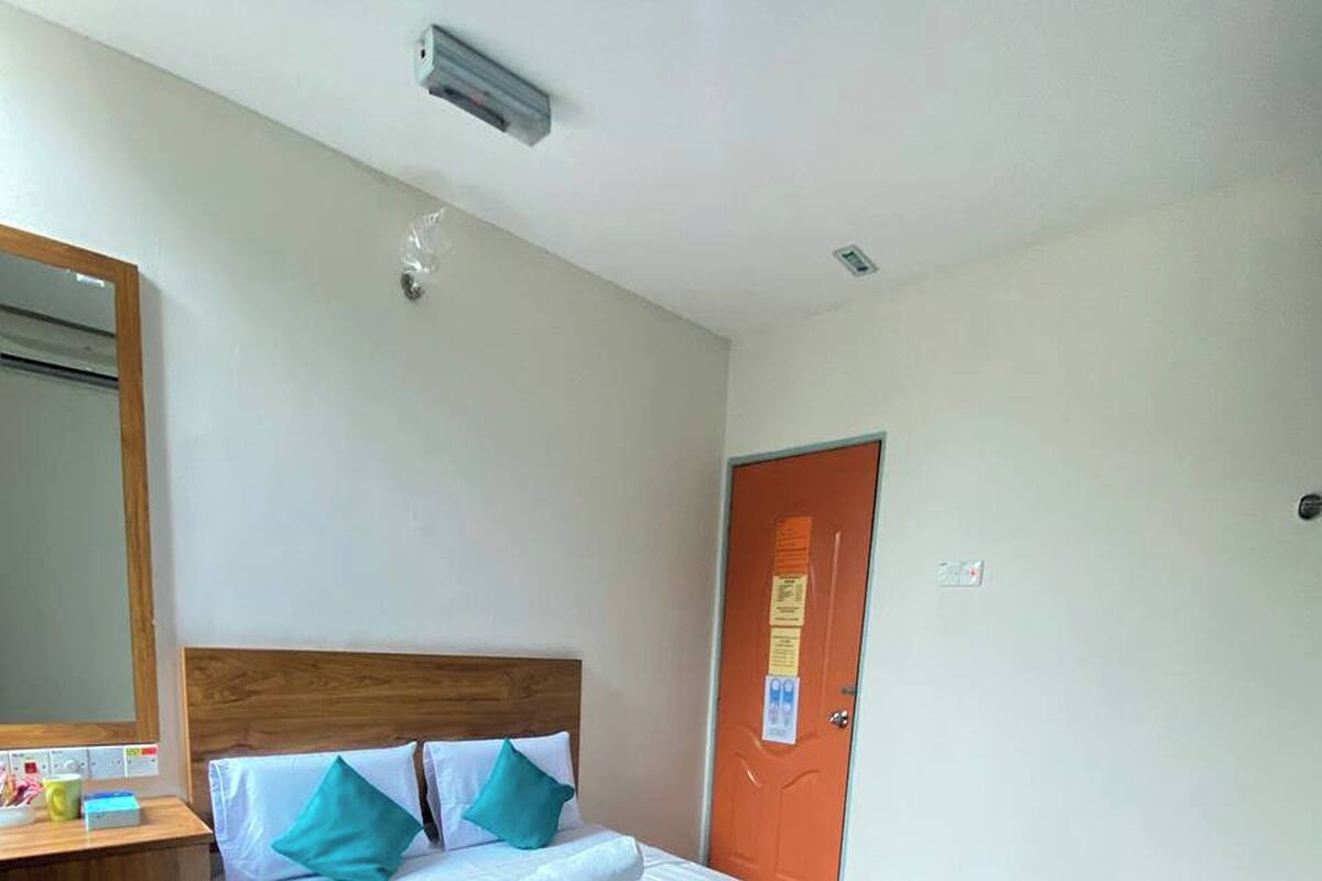 Quarto de hotel com cama, cabeceira de madeira, mesa de cabeceira, espelho, porta e uma pequena mesa.