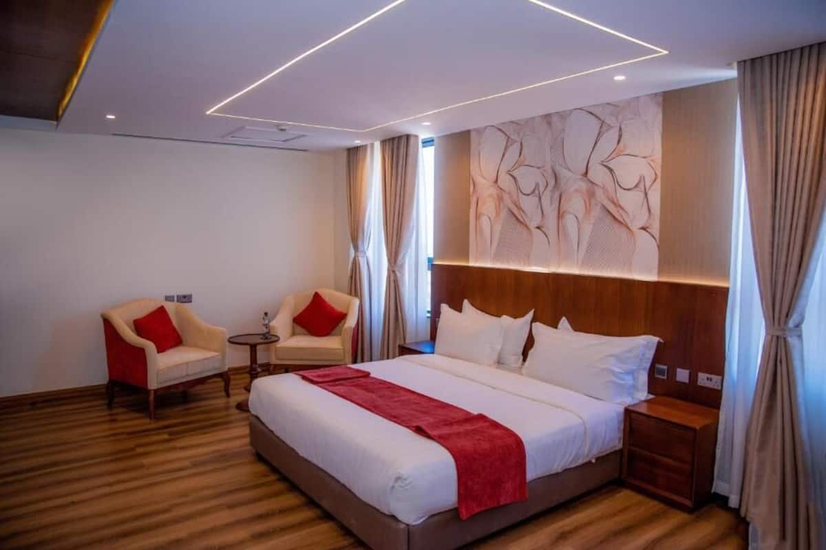 Quarto de hotel com uma cama grande, duas poltronas, uma mesinha e uma mesa de cabeceira.